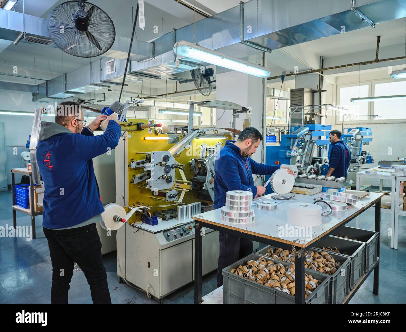 people working in a sticker printing factory. worker uses a stickier ...