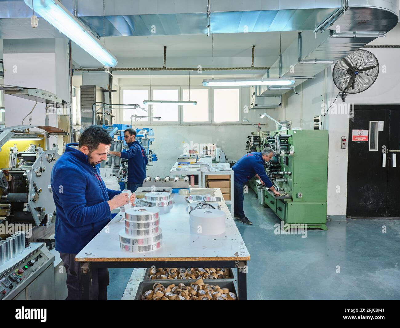 people working in a sticker printing factory. worker uses a stickier ...