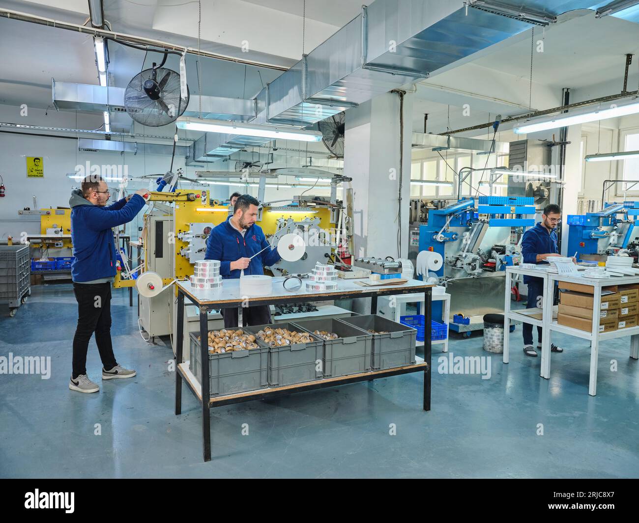 people working in a sticker printing factory. worker uses a stickier ...