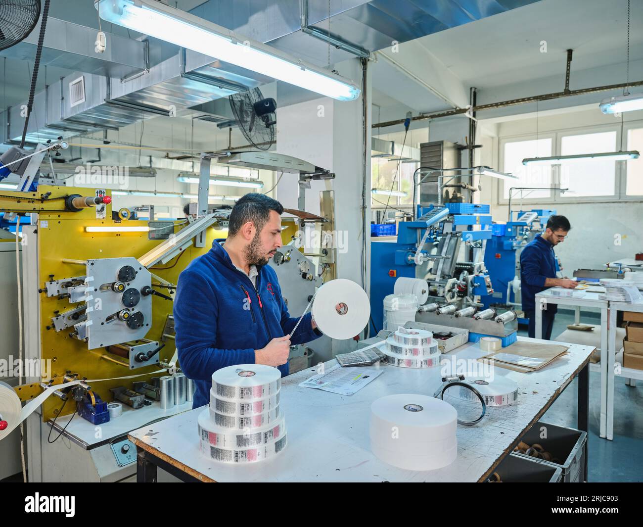 people working in a sticker printing factory. worker uses a stickier ...