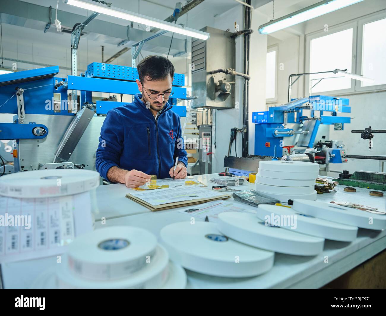 people working in a sticker printing factory. worker uses a stickier ...