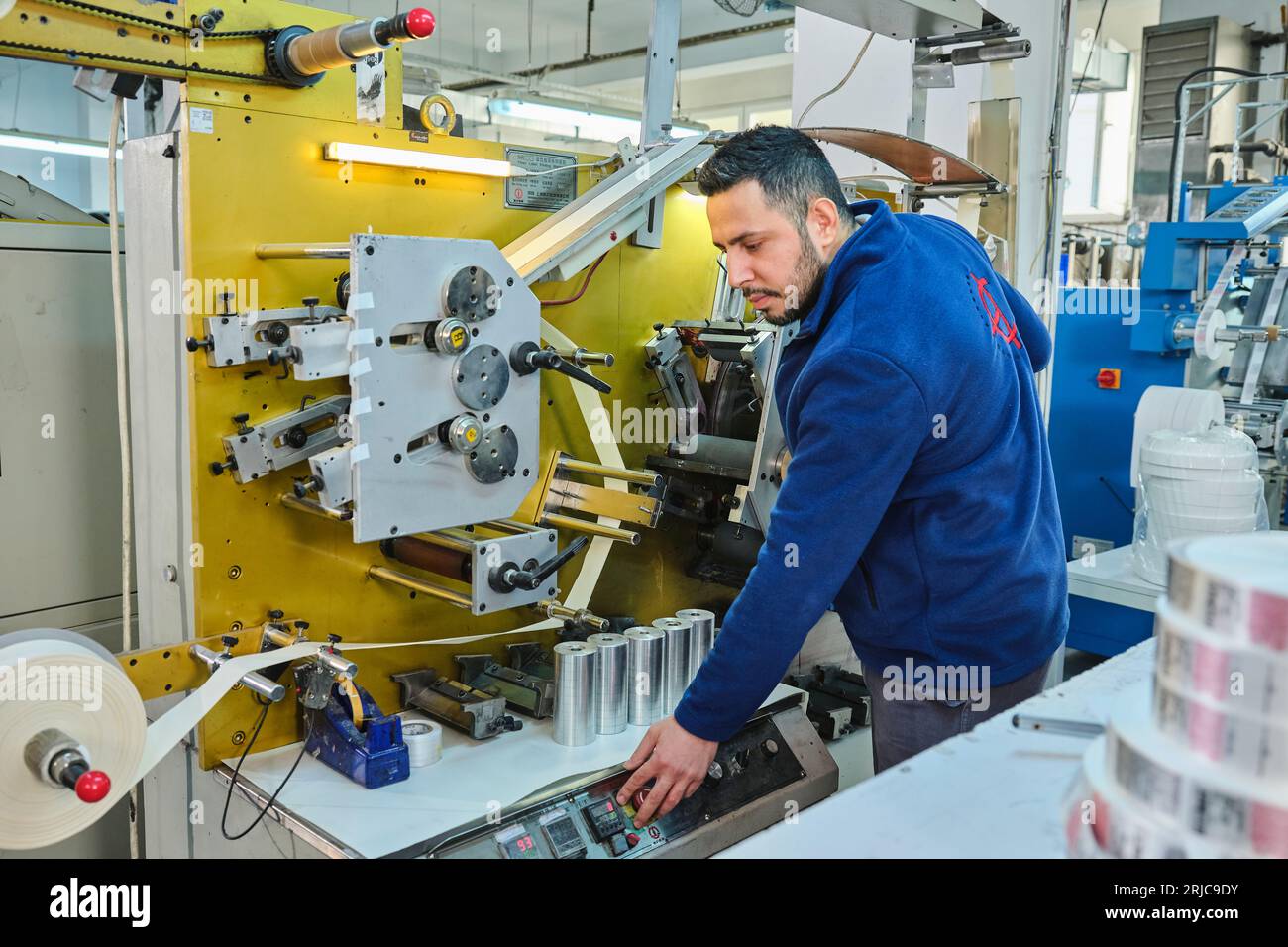 people working in a sticker printing factory. worker uses a stickier ...