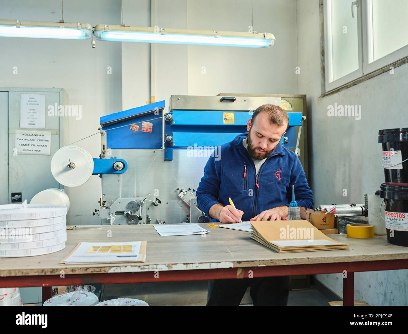 people working in a sticker printing factory. worker uses a stickier ...