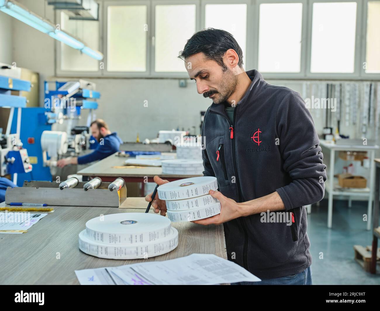 people working in a sticker printing factory. worker uses a stickier ...