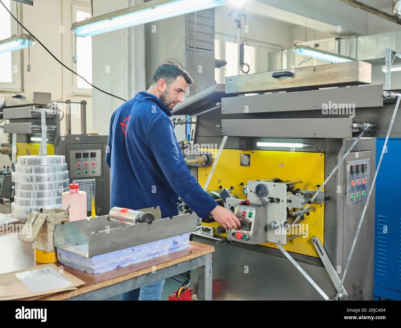 people working in a sticker printing factory. worker uses a stickier ...