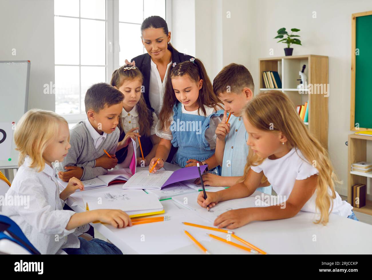 Concentrated children and teacher together draw standing around table ...