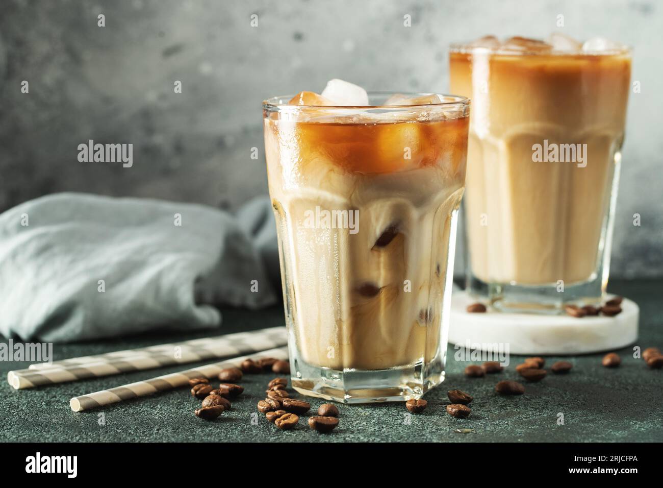 Ice coffee in a tall glass with cream poured over, ice cubes and beans ...