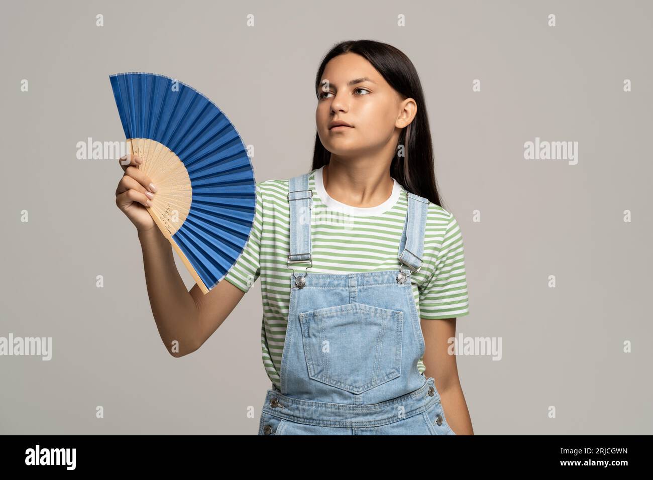 Teen girl waving blue fan in hand. Tanned stylish teenager languishing ...