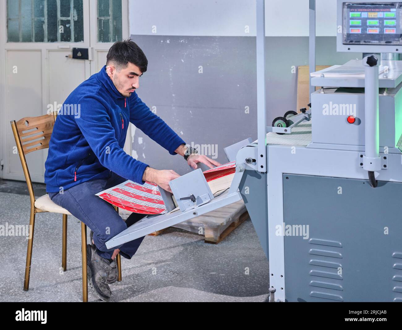 people working in a sticker printing factory. worker uses a stickier ...