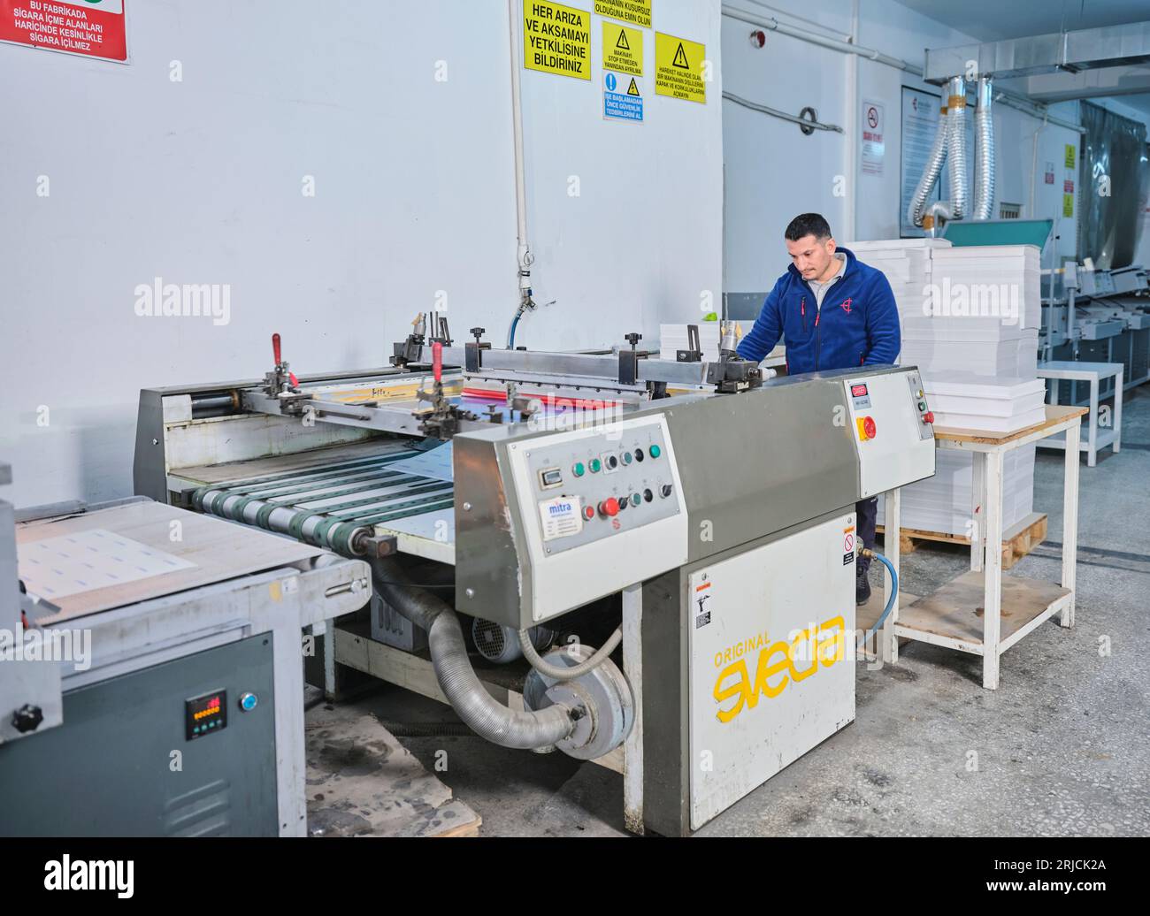 people working in a sticker printing factory. worker uses a stickier ...