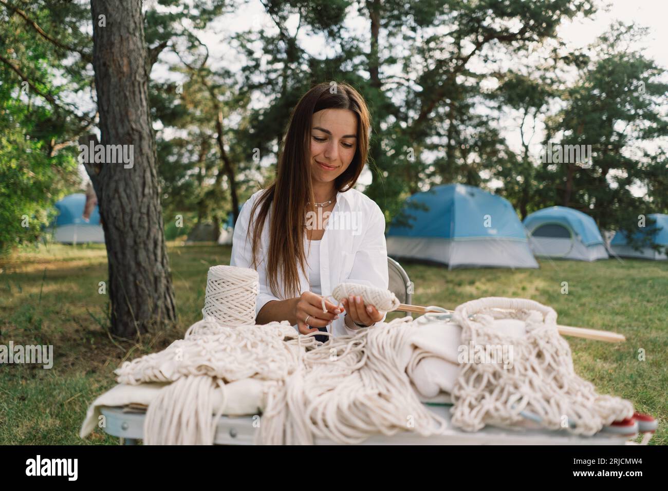 Woman knits bag using macrame technique outdoors near tents. Outdoor ...