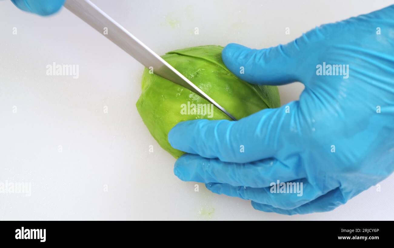Ripe avocado cutting close up on white kitchen board. Chef hands in ...