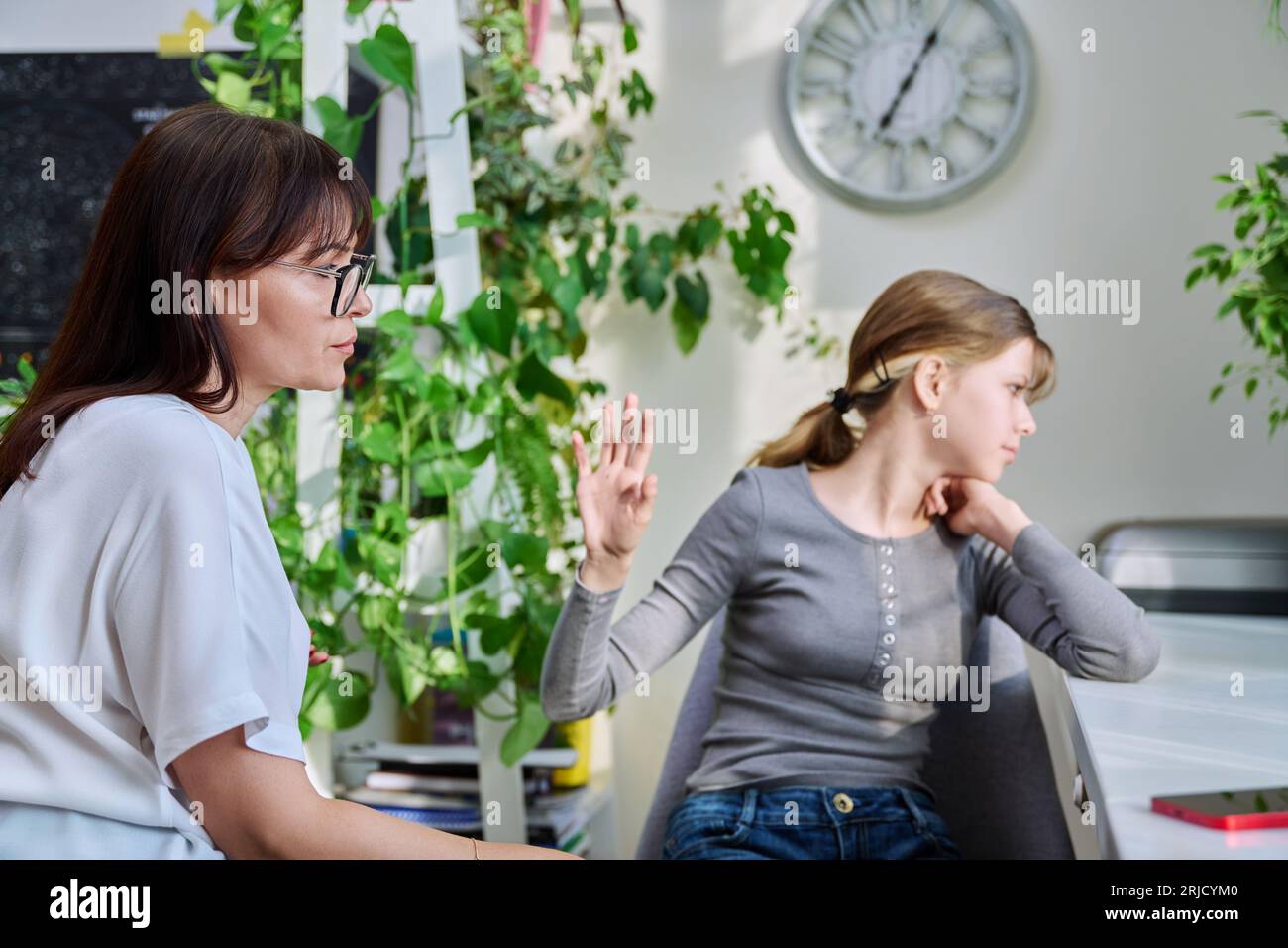 Upset mother and teenage daughter sitting together at home in room ...