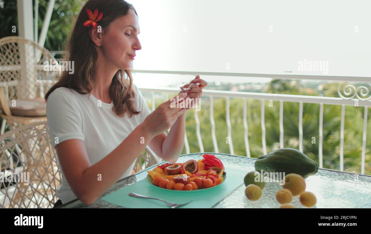 Woman eating tropical fruits sitting on the balcony with jungle view ...