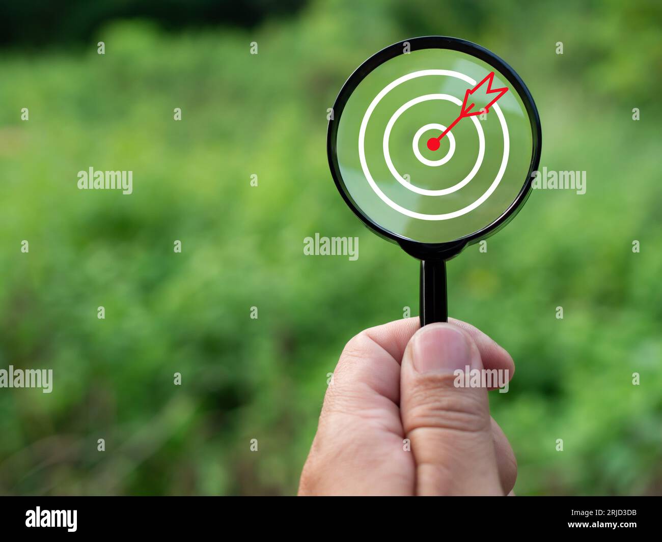 Human hand holding a magnifying glass with target icon on green nature ...