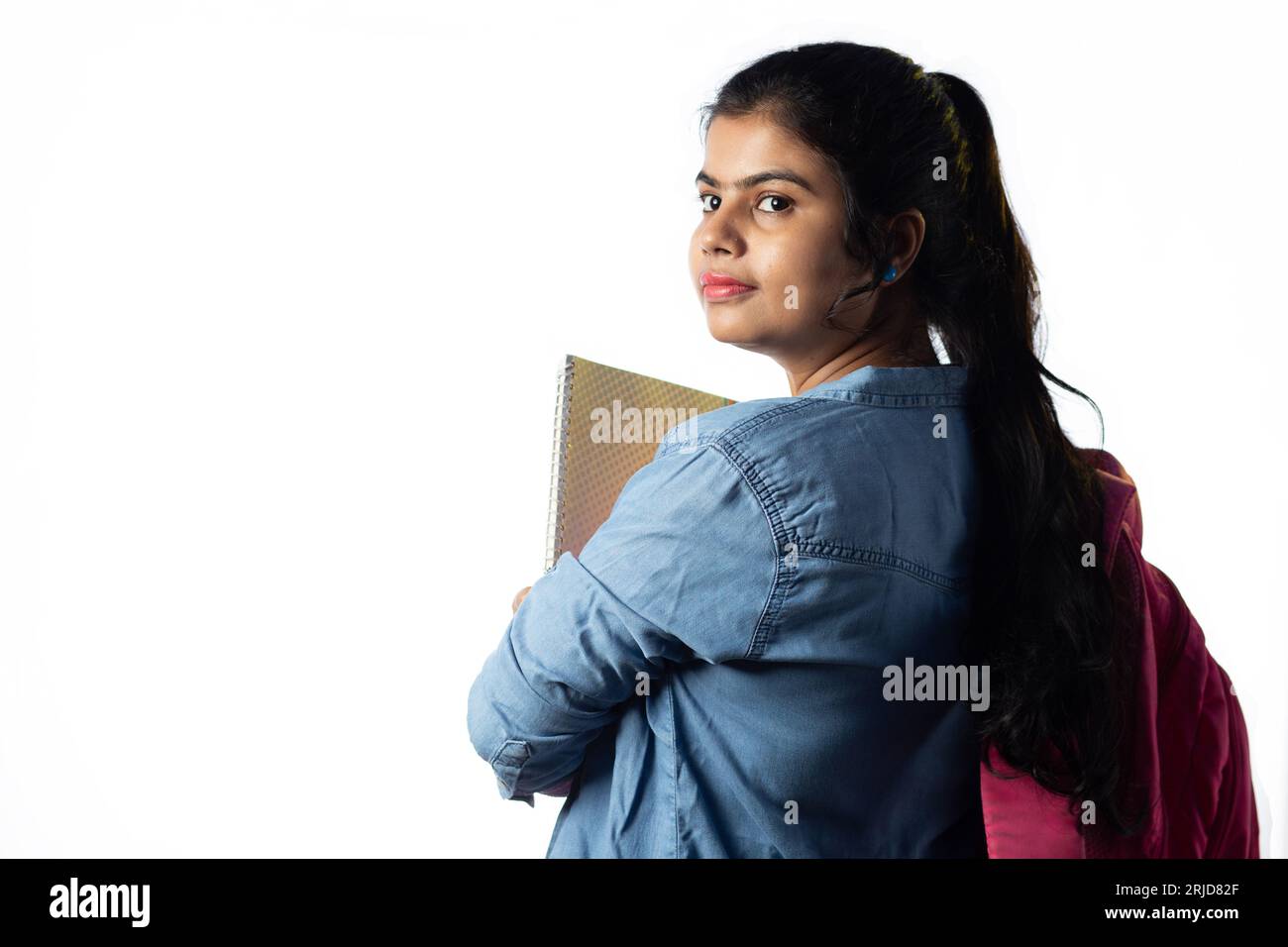A pretty young Indian girl with books in hand and backpack looking back ...
