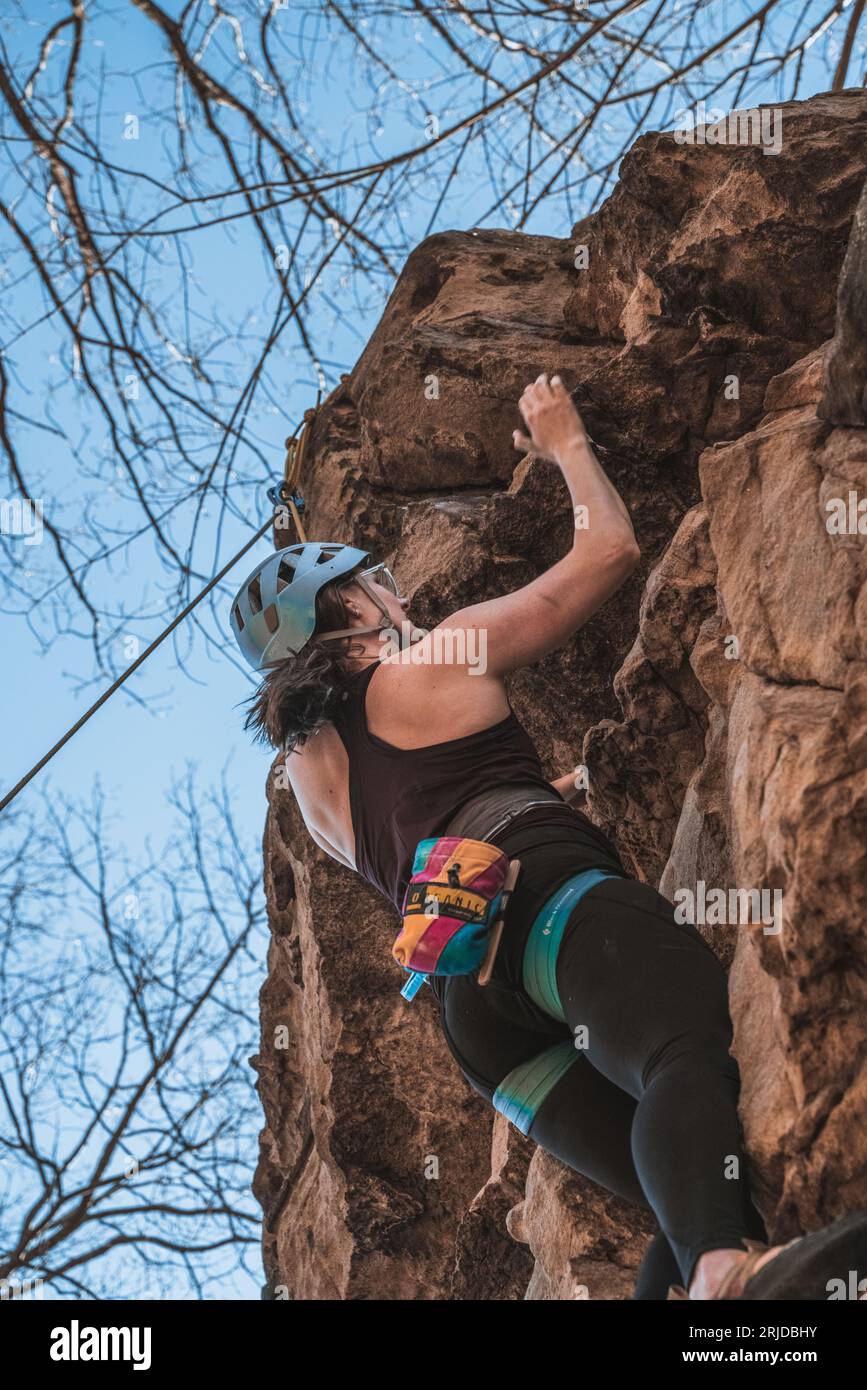 A woman is rock climbing outdoors in Western Pennsylvania, her face ...
