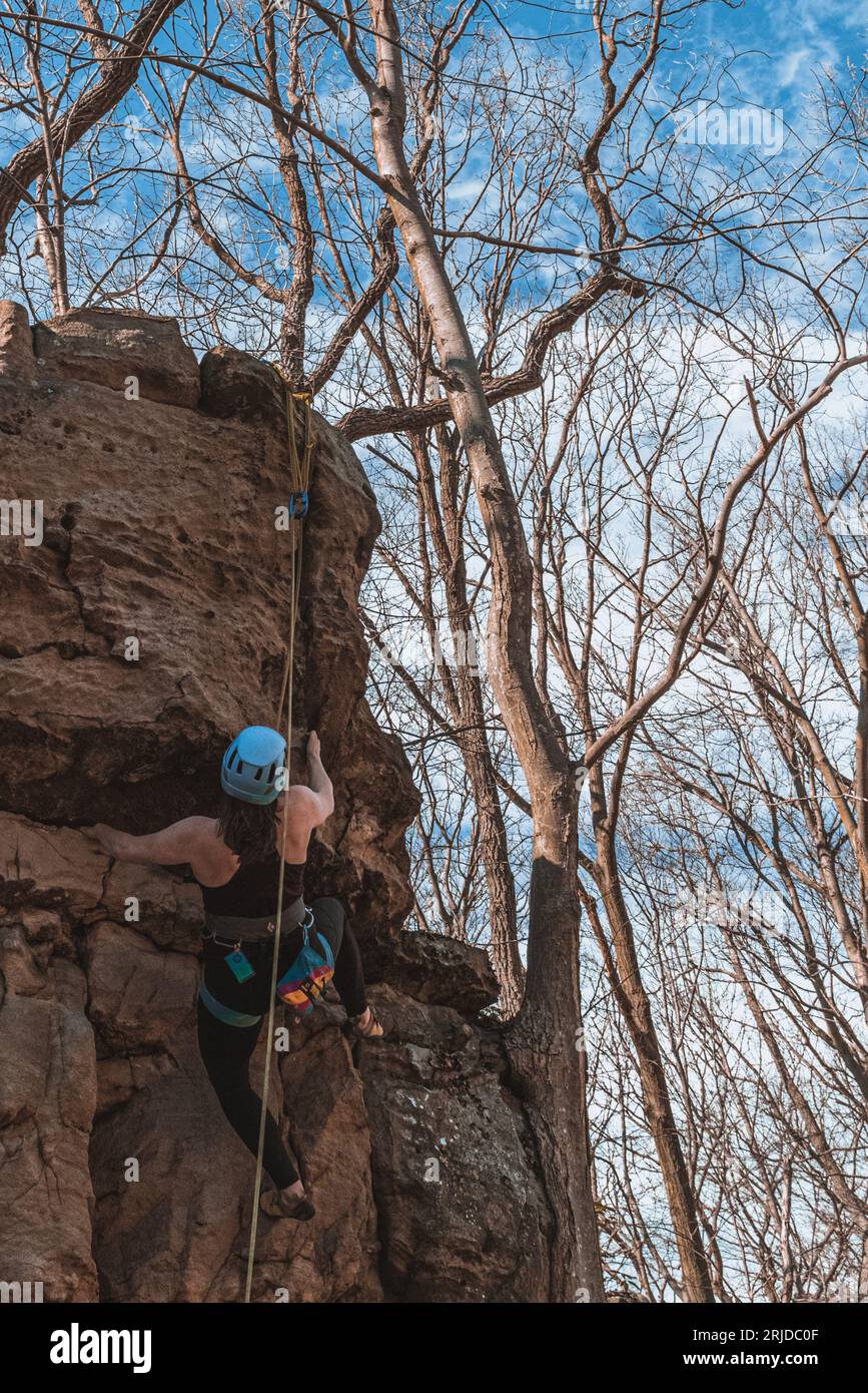 A female rock climber scaling a rocky cliff face using a rope and ...