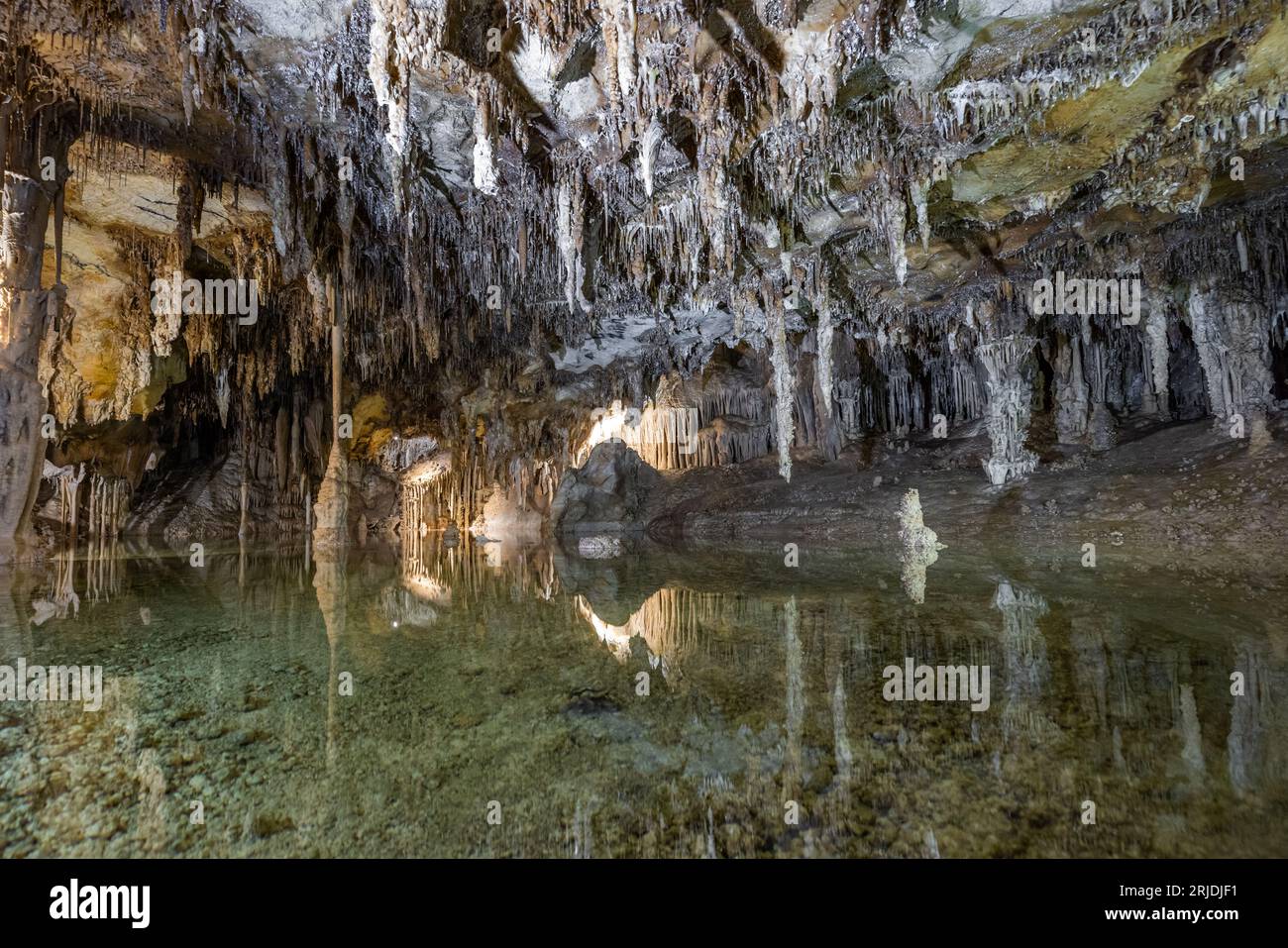 Underground pool with calm reflections with stalactites hanging from ...