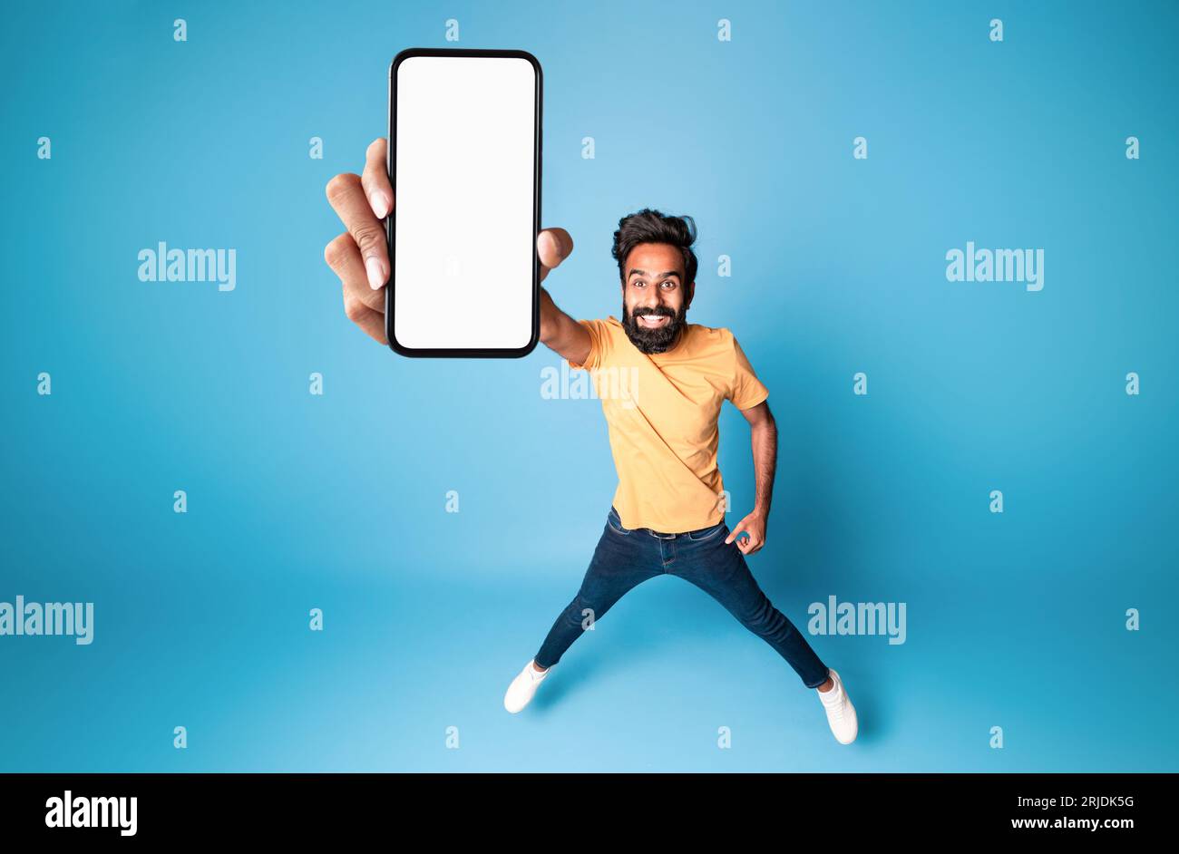 Happy indian man showing empty smartphone screen, jumping up over blue ...