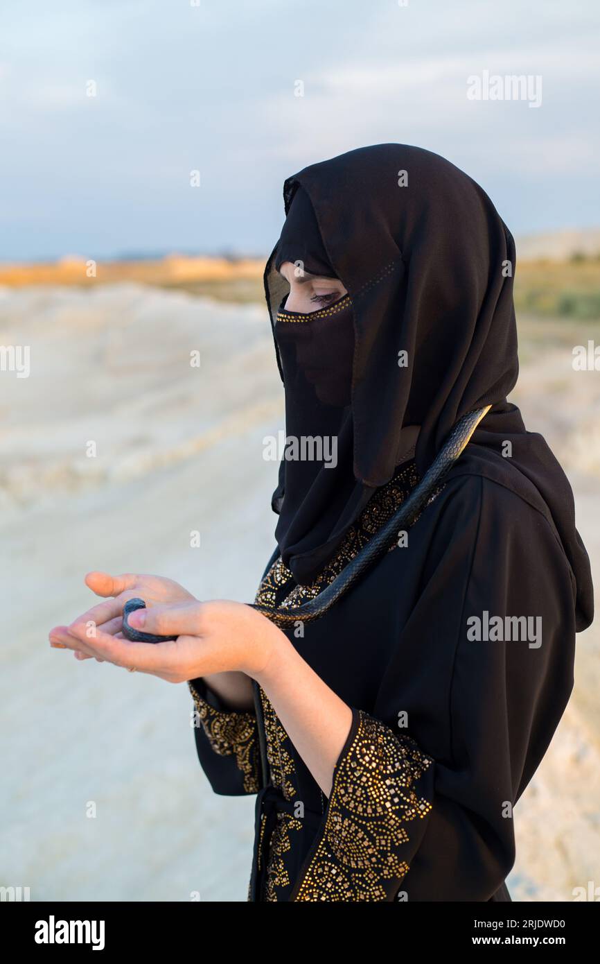A Muslim woman in national dress holds snake in her hands while ...