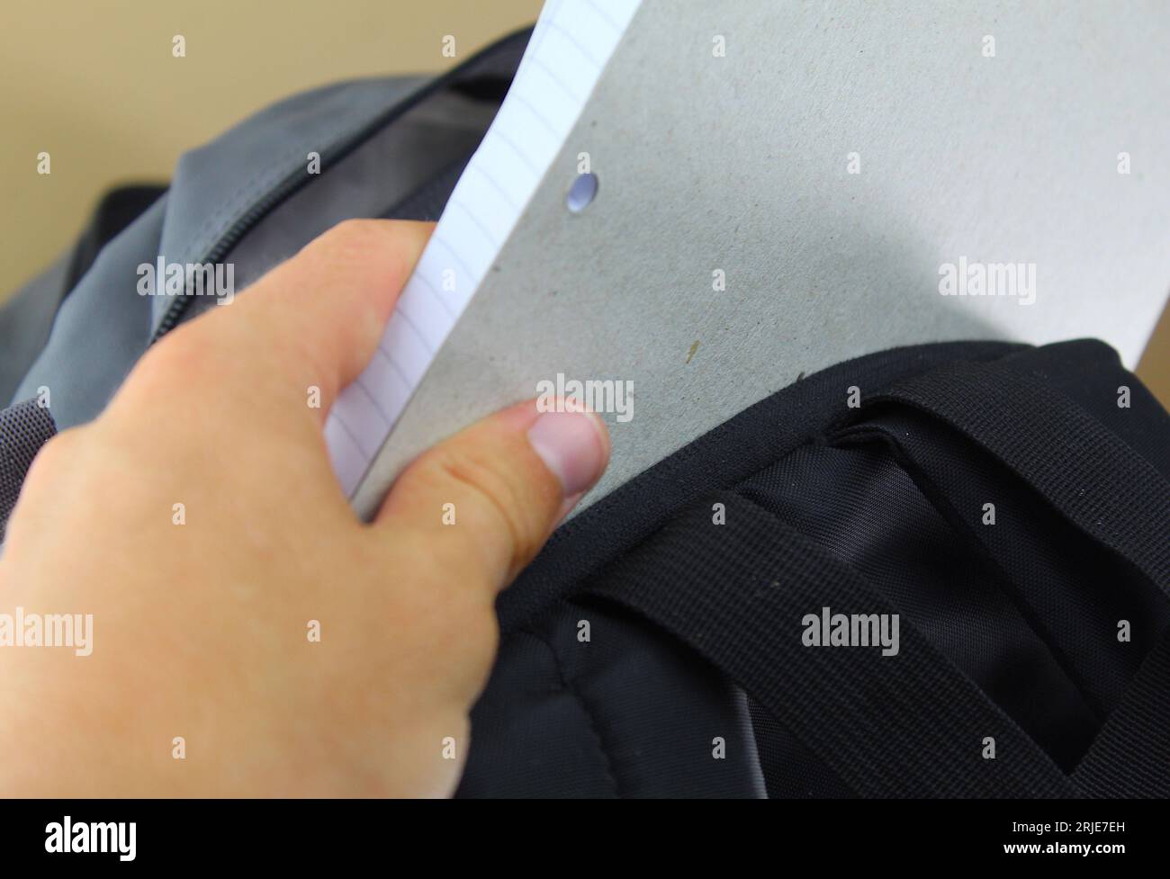 A photo of a white student putting his notebook of paper into his grey ...
