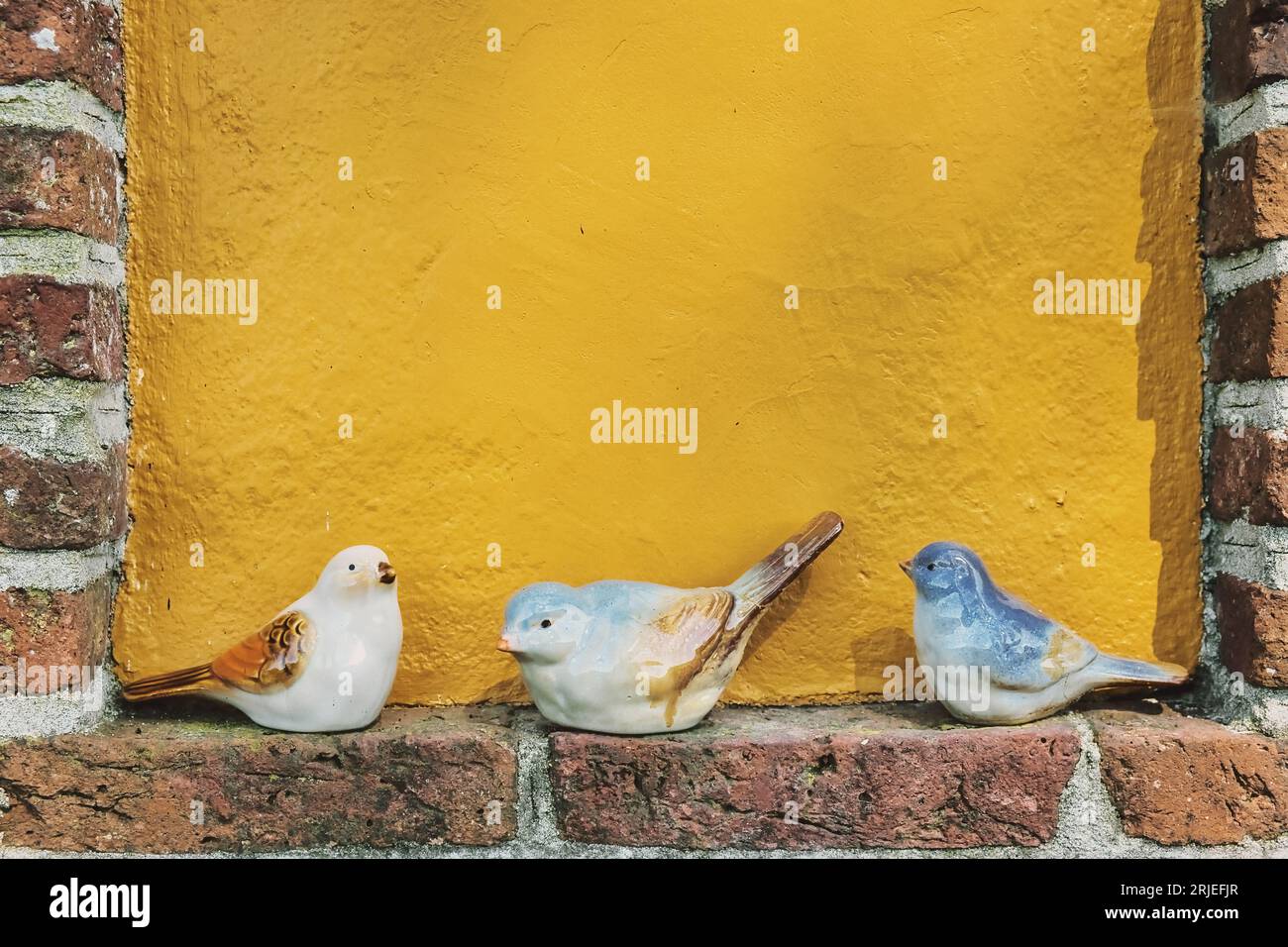 Three ceramic birds in a brick niche with a yellow background Stock ...