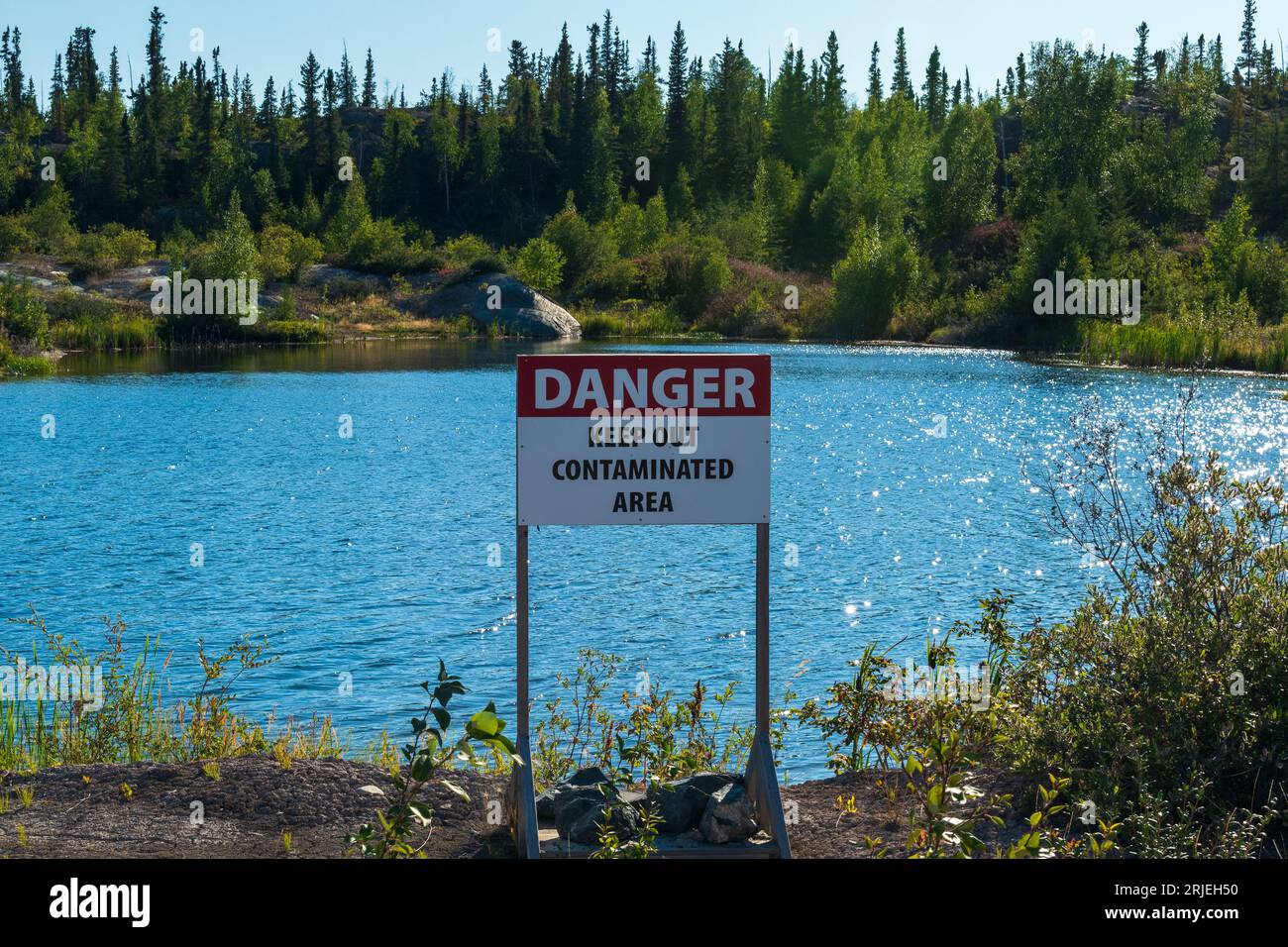Beautiful tree-lined blue lake, with cautionary contamination sign ...