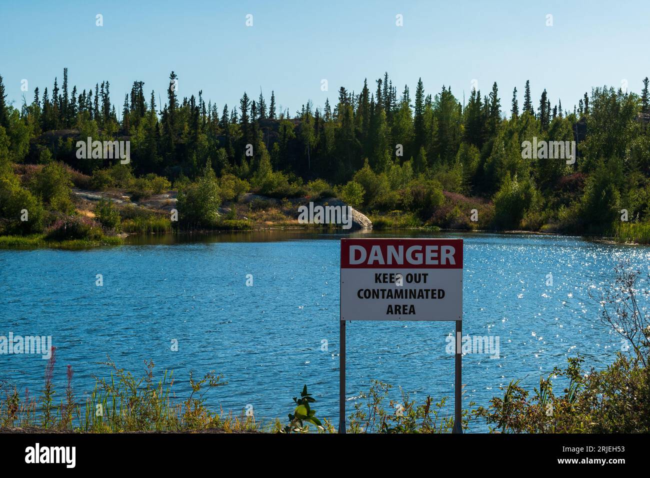 Beautiful tree-lined blue lake, with cautionary contamination sign ...