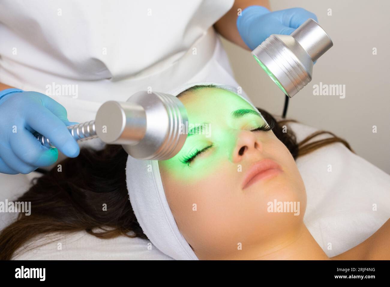 Specialist in work uniform does light therapy procedure on woman client ...