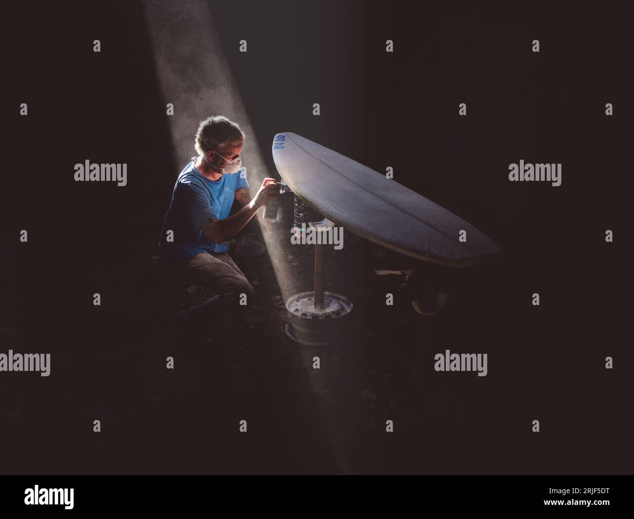 High angle of male master spraying aerosol on surfboard while sitting ...