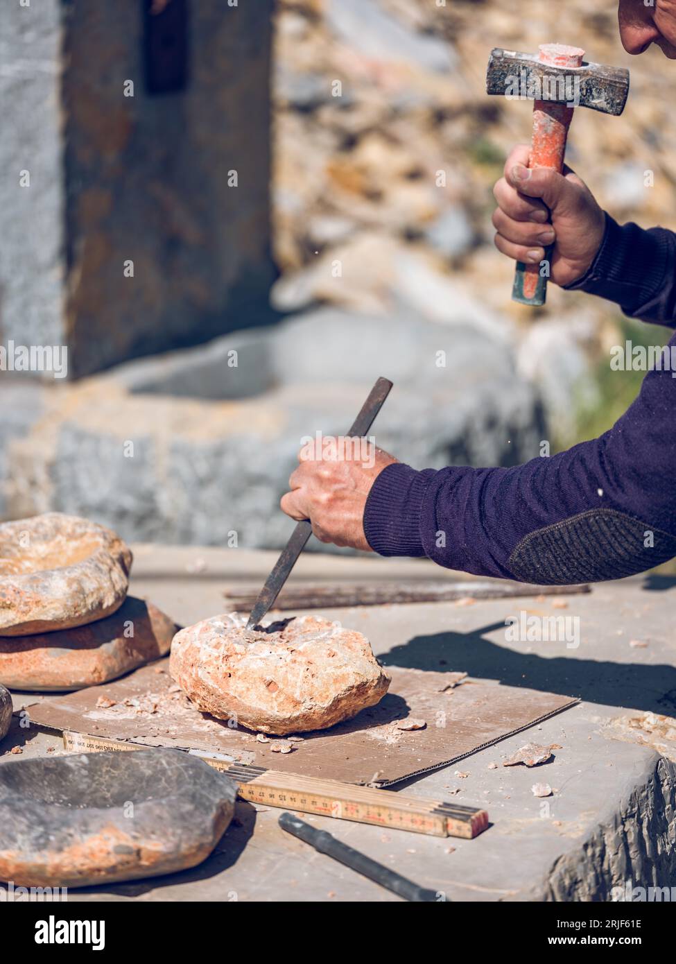Crop anonymous craftsman cutting rock using chisel and hammer while ...