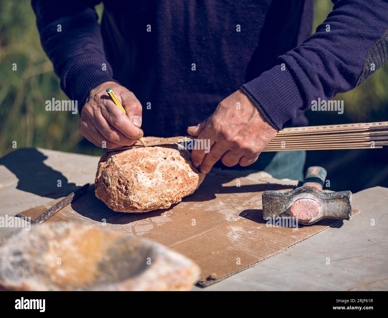 Crop unrecognizable mature craftsman making marks on solid rough stone ...
