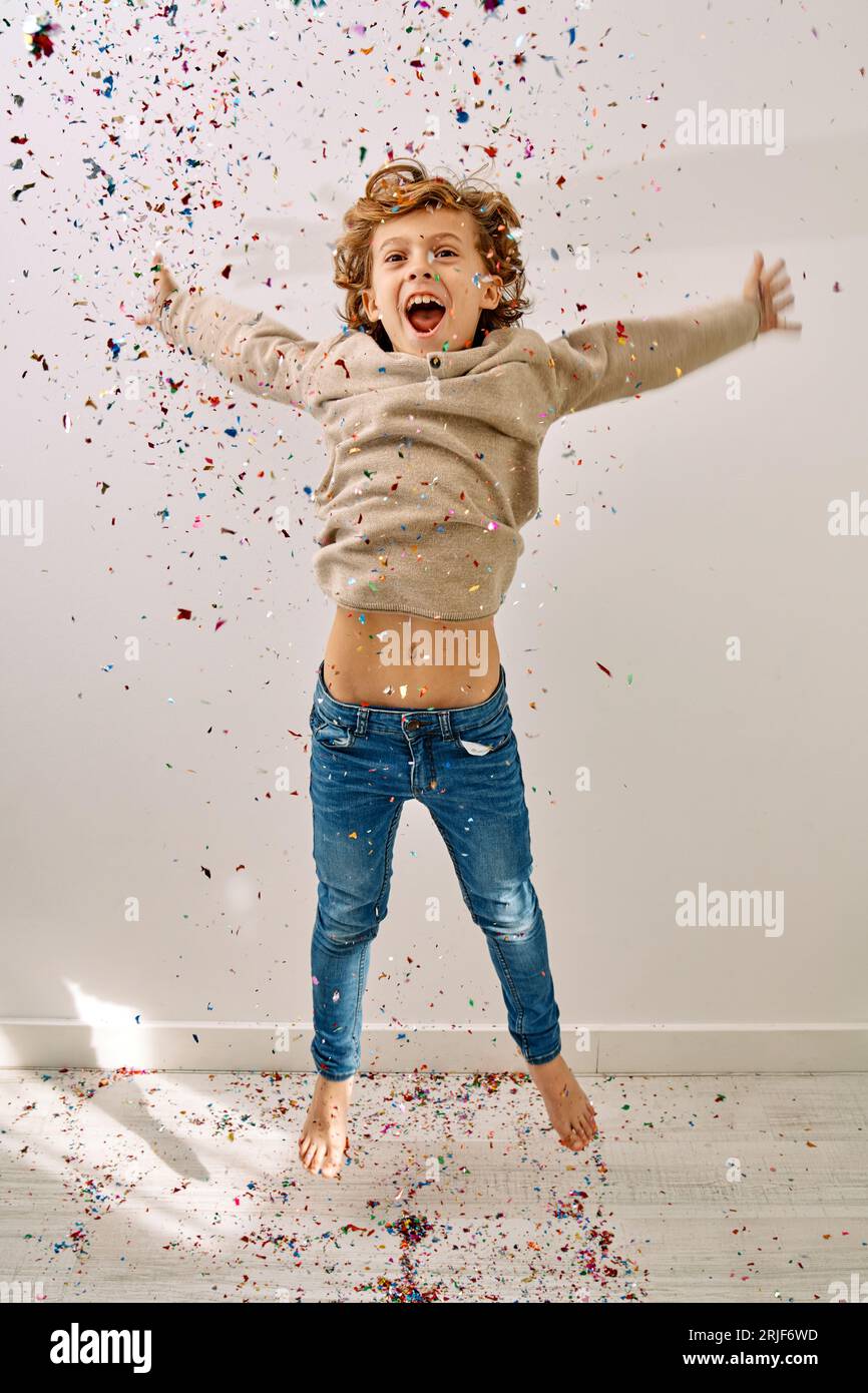 Full body of cheerful preschool boy in jeans and jumper jumping with ...
