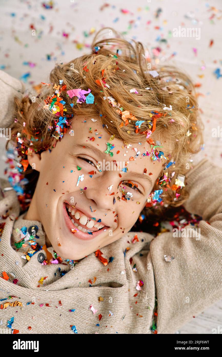 Happy blond kid smiling and looking at camera in confetti with hands on ...