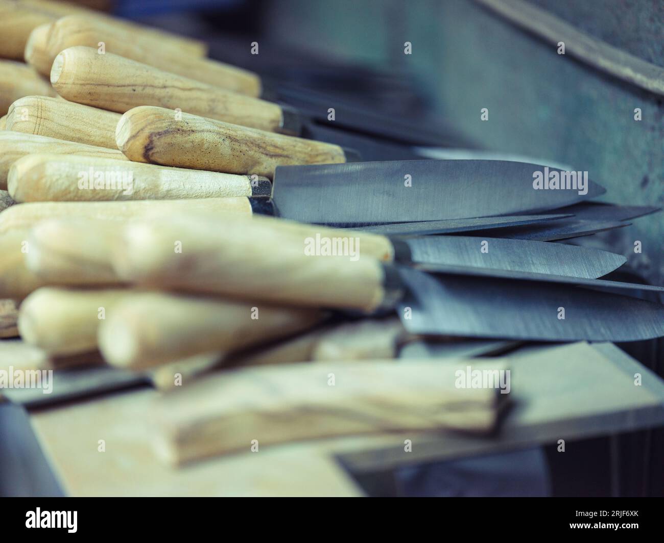 Heap of new steel knives with wooden handles placed on workbench in ...