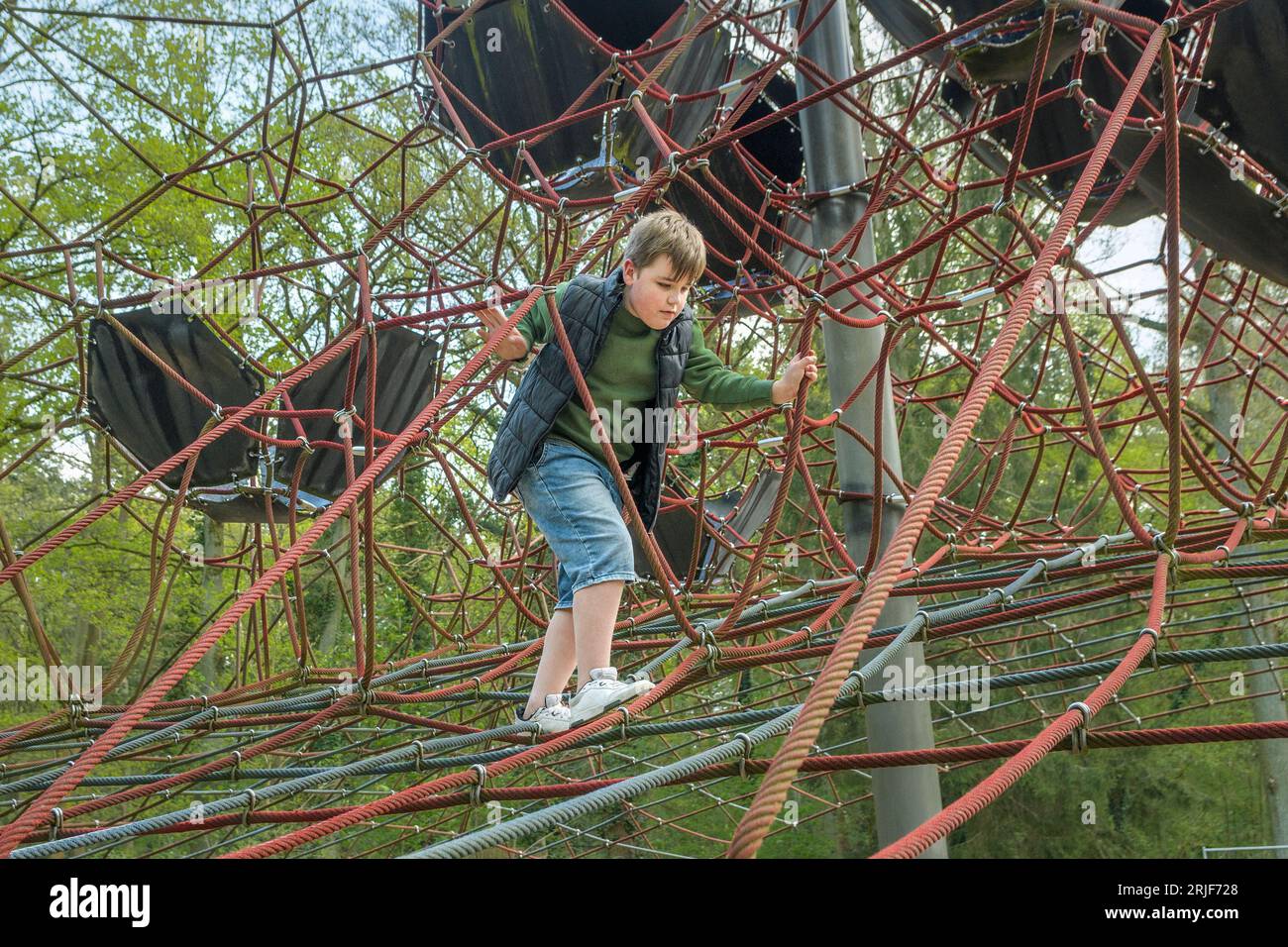 Teenage boy climbing on spider web with expression in public park ...