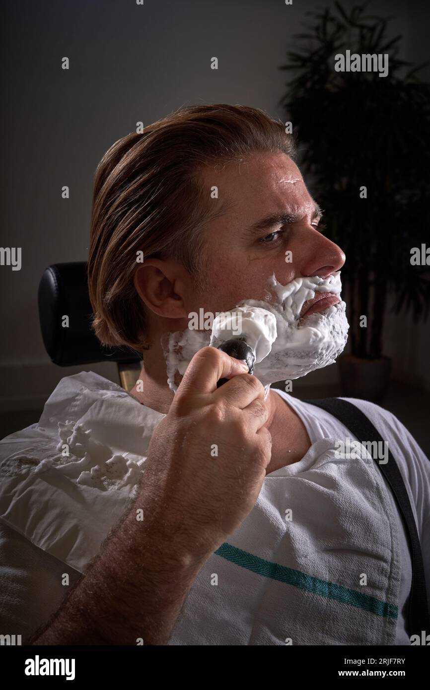 Serious male client in white wear applying white shaving foam on beard ...