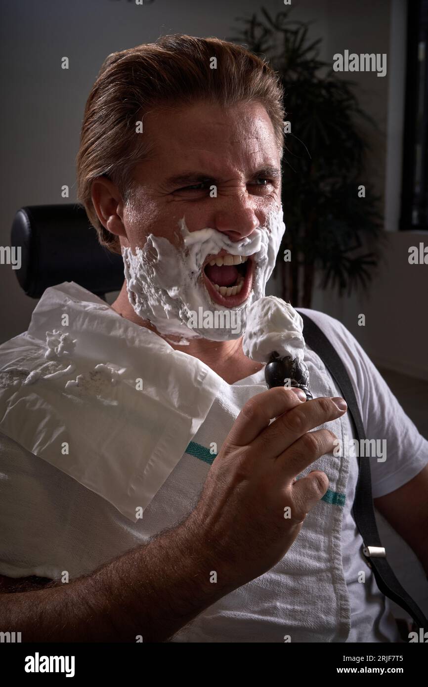 Male client with foamy beard pretending to sing into brush with white ...