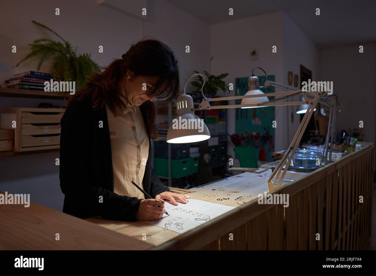 Side view of concentrated female jeweler drawing sketches on paper ...