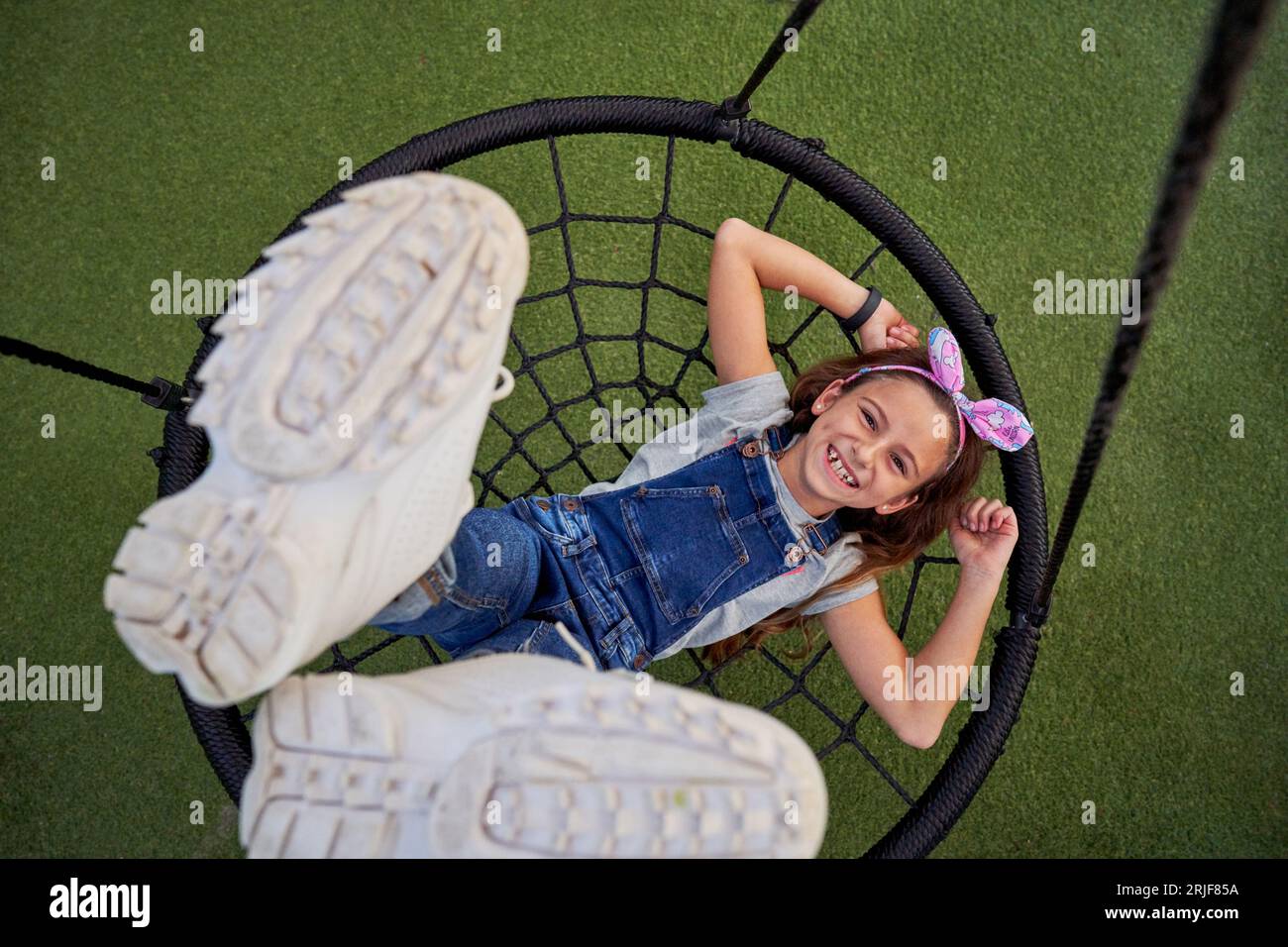 Top view of joyful kid in overall looking at camera while lying on web ...