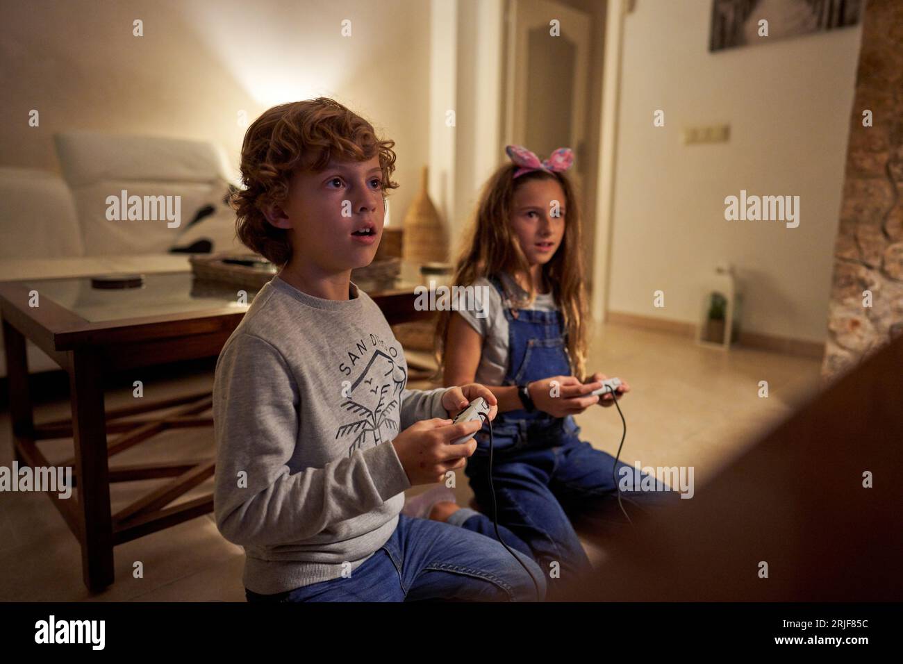 Baffled curly haired boy and girl with long hair in jeans playing video ...