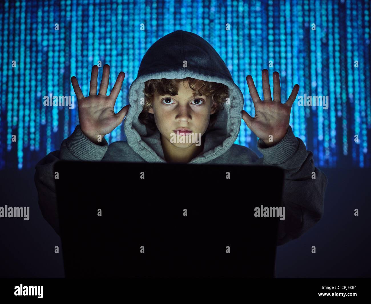 Boy hacker with hands up sitting at laptop on blurred binary code ...