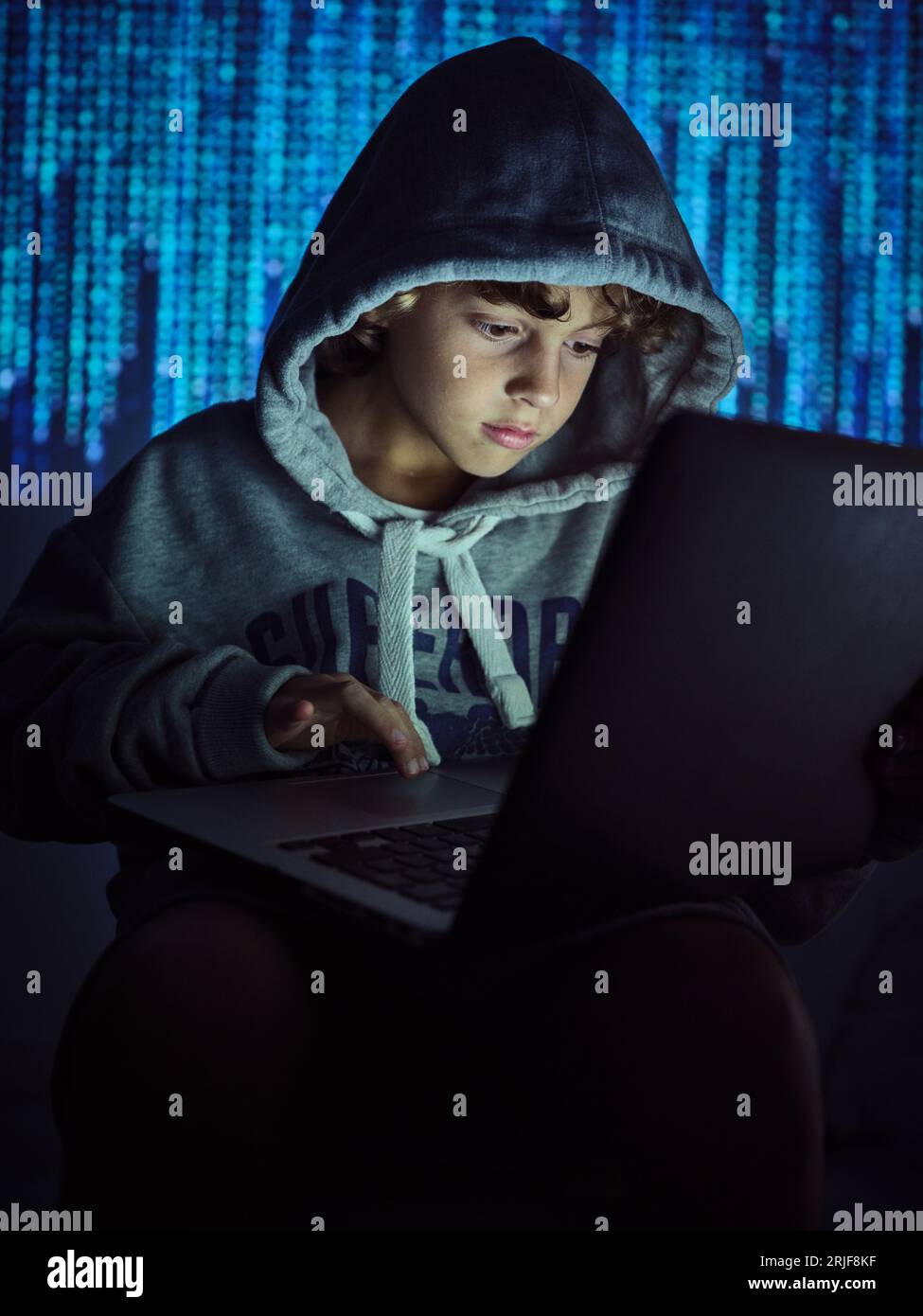 Crop kid hacker typing on laptop while making cyber crime blurred binary code background in dim ...