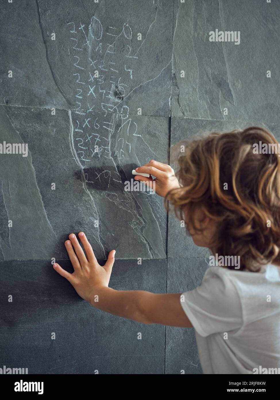 Back view of intelligent kid solving math equations on on black stone ...