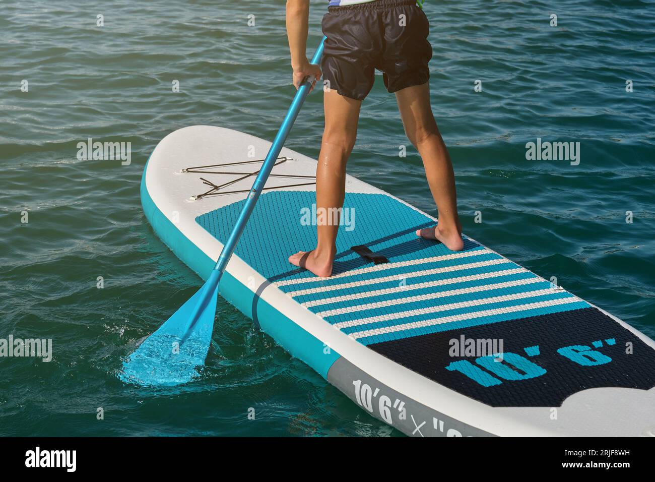 Crop anonymous boy standing on SUP board and paddling in middle of sea ...