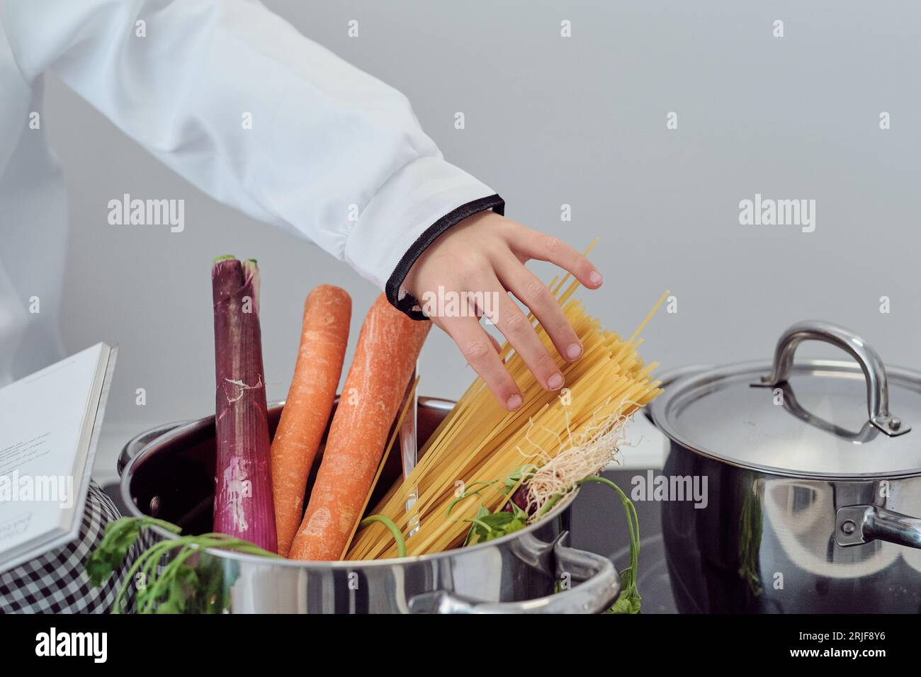 Crop anonymous preteen boy in chef uniform putting spaghetti into ...