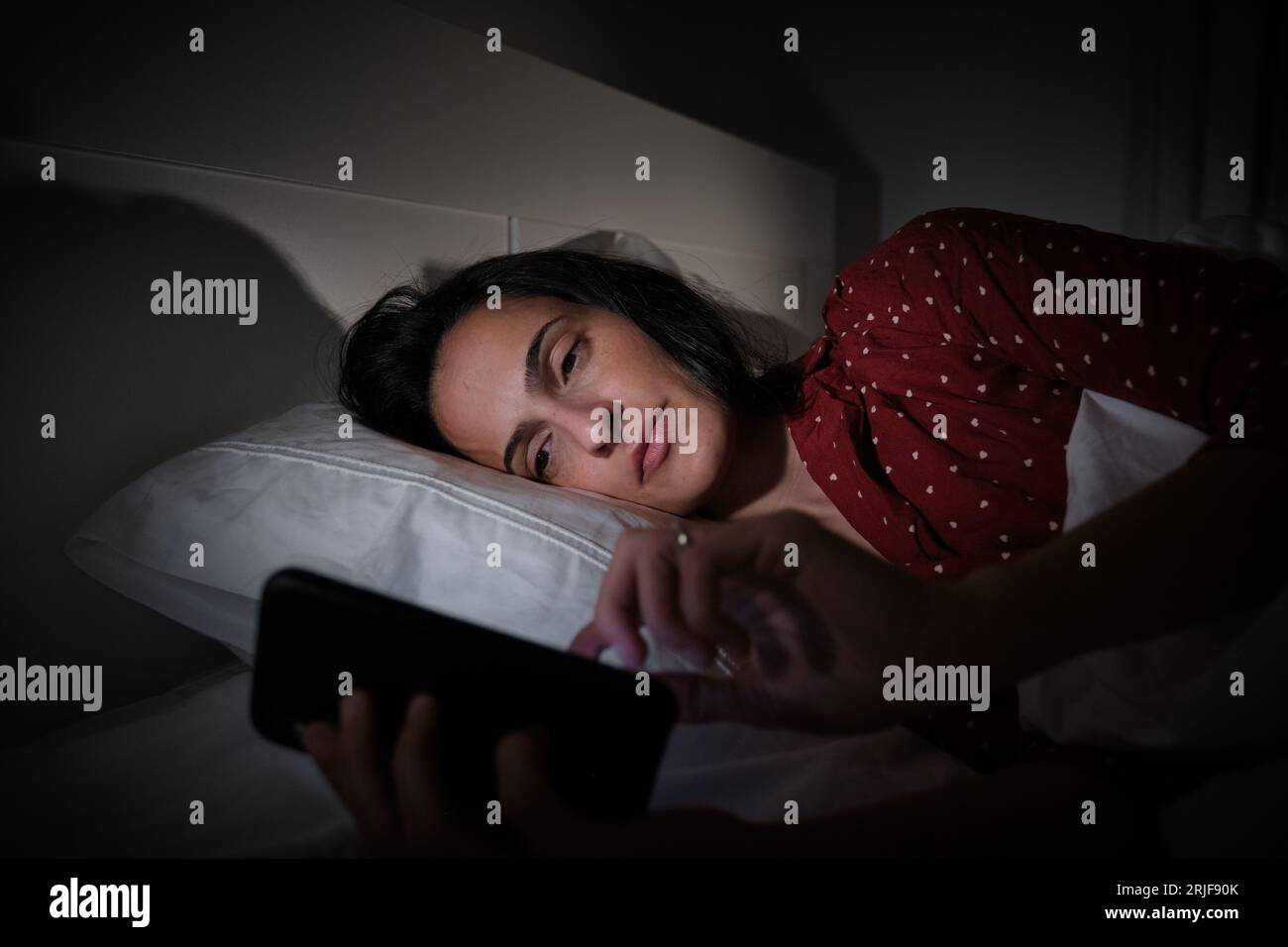 Focused Hispanic female in sleepwear text messaging on modern cellphone ...