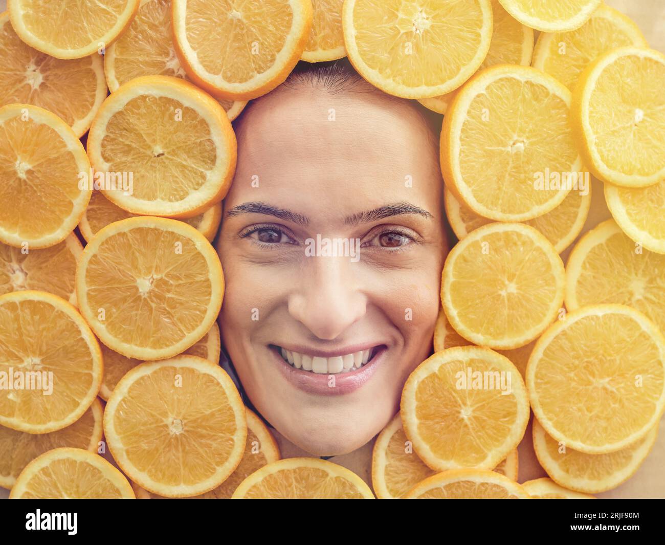Slices of ripe healthy juicy oranges placed around face of happy female ...