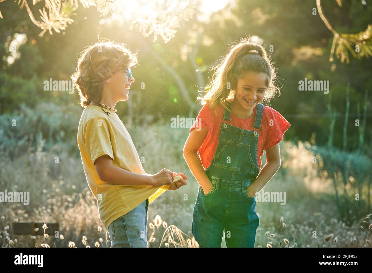 Happy boy and girl with hands in pockets telling jokes while standing ...